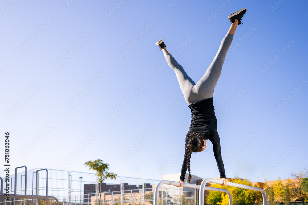 back view of fit woman doing handstand with splits on parallel bars ...