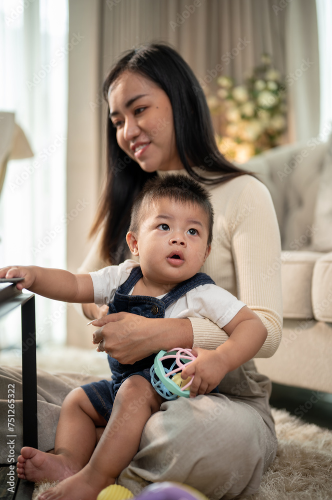 A cute Asian baby boy is sitting on his mom's lap and playing with toys ...