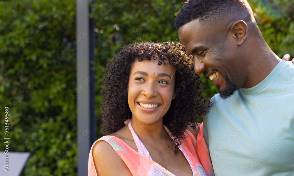 Biracial couple smiles warmly, standing close in an outdoor setting at ...