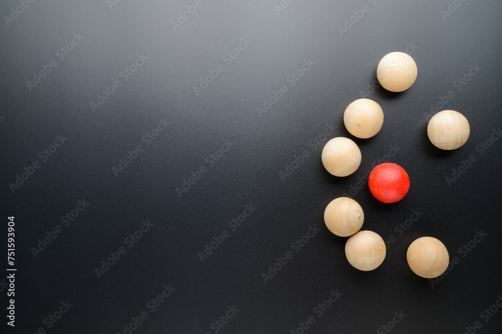 Small red ball is under seige of many wooden balls on black background ...