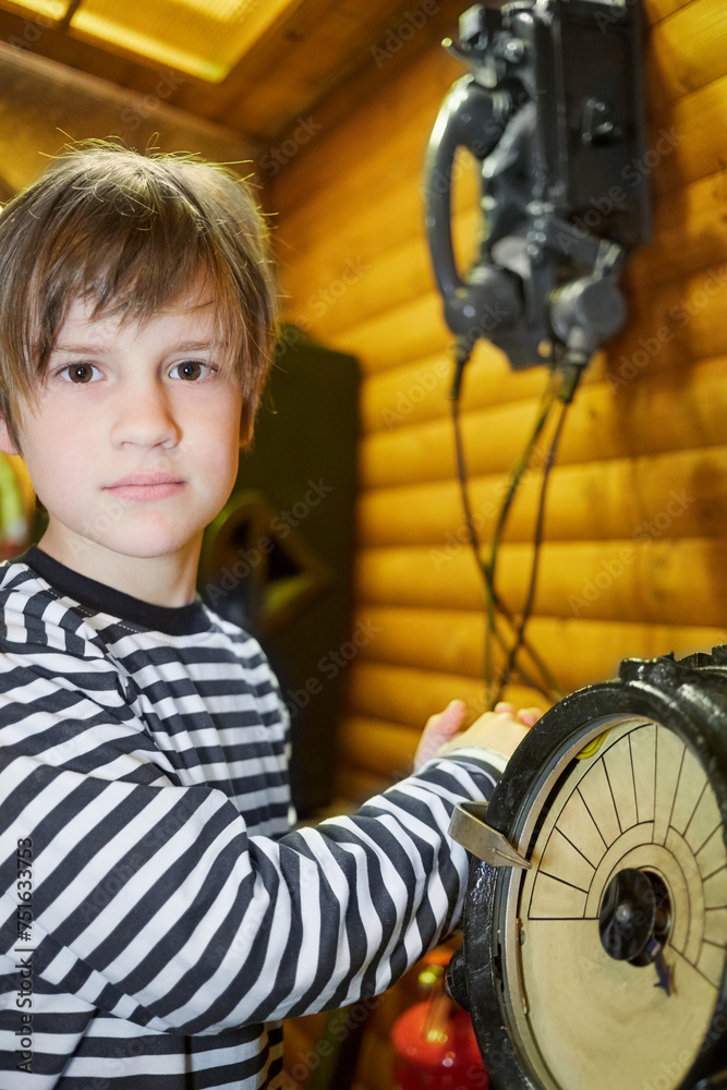 Boy in striped vest stands near ship engine telegraph at pleasure boat ...