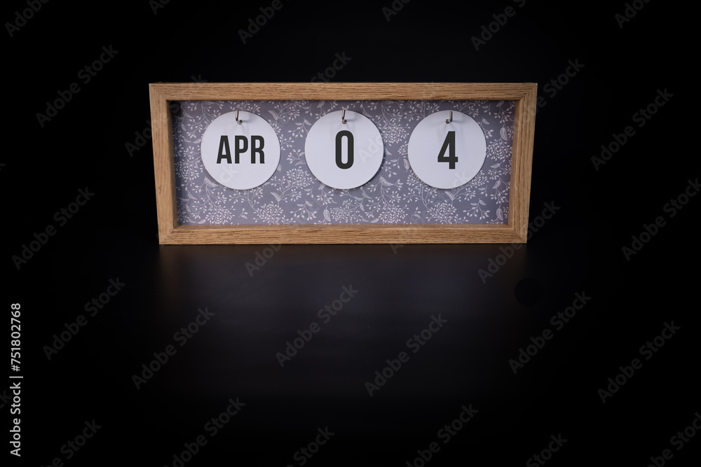 A wooden calendar block showing the date April 4th on a dark black ...