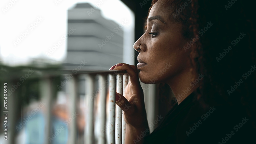 Profile close-up of a serious black woman leaning ln metal bar by home ...