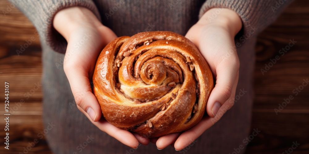 Top view of female baker's hands holding a twisted cinnamon bun in a ...