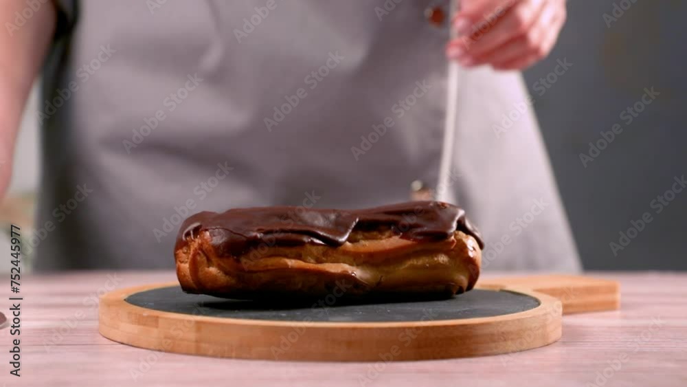 Womans hands cuts French eclair on the table. A woman shows a cross ...