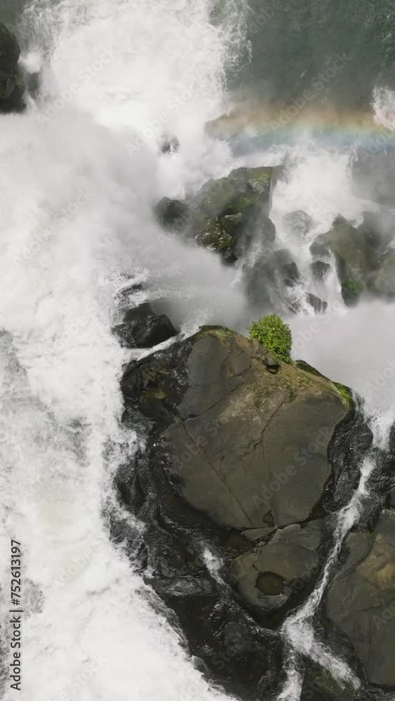 A rainbow over the stream of waterfalls from high rocks, splitting into ...