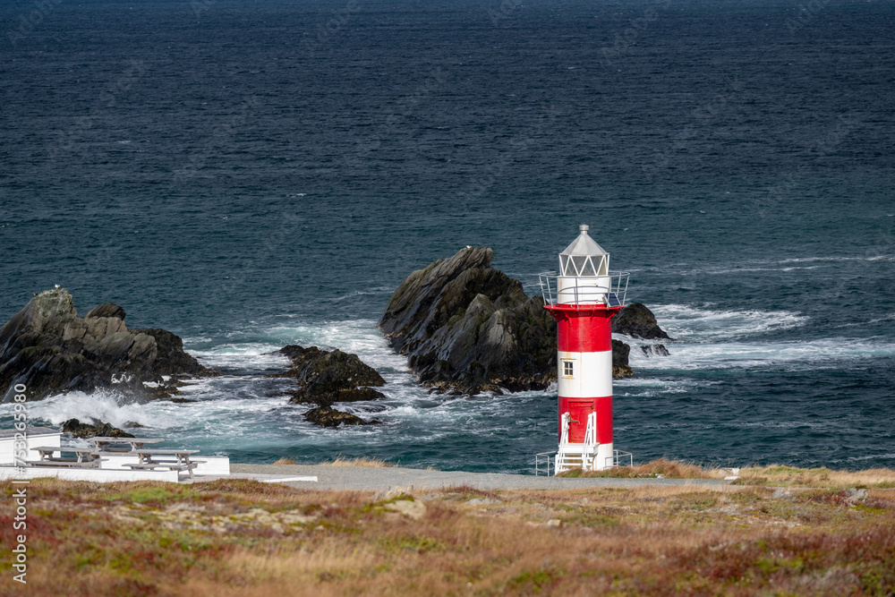 A tall circular lighthouse tower has horizontal red and white colors ...