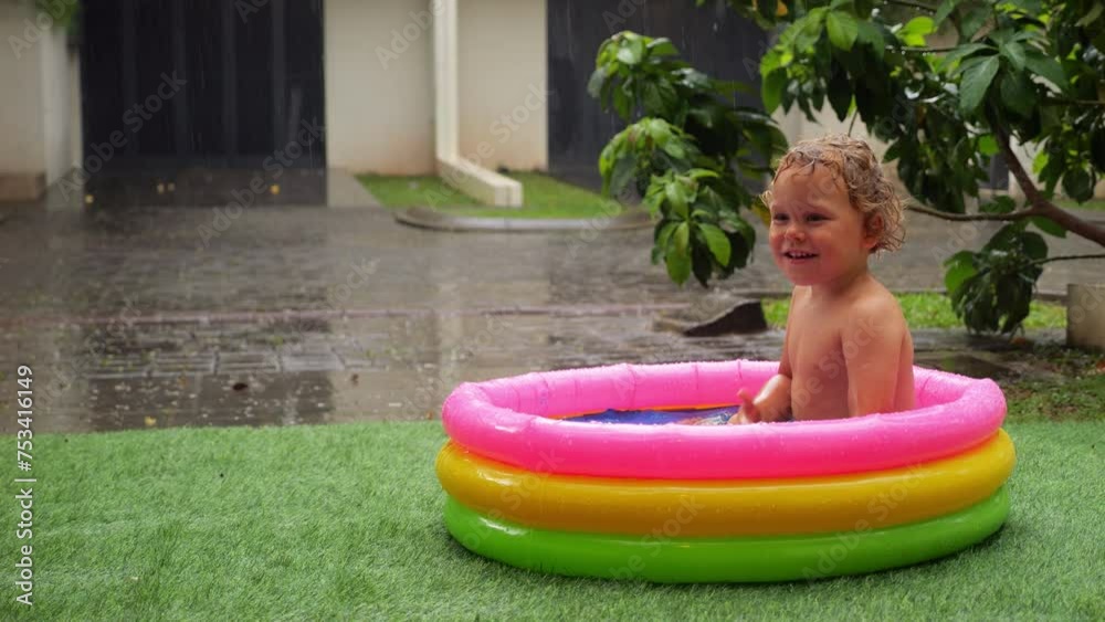 Vidéo Stock Toddler sits in small inflatable pool under tropical rain ...