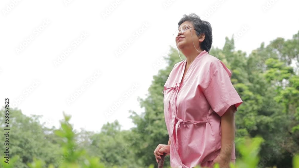 An elderly Asian female patient walks using a cane to support herself ...