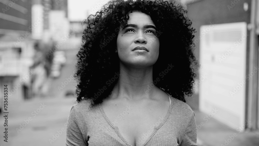 One hopeful young black woman with curly hair standing in street ...