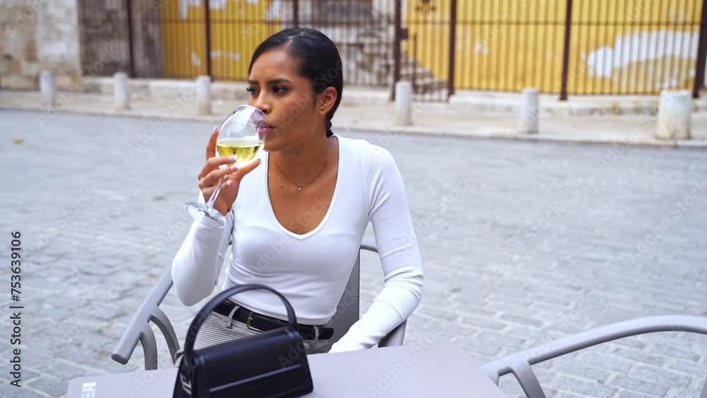 Young hispanic woman drinking wine outside in cafe patio while ...