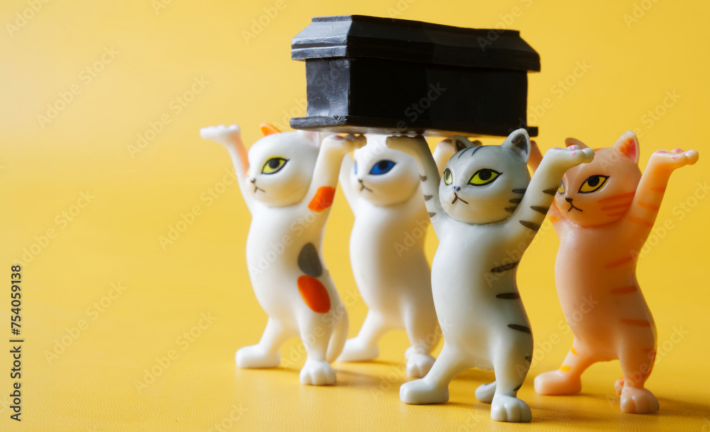 Toy dancing cats carrying a black coffin on their feet. A mock concept ...