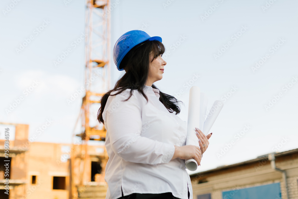 Plus size female engineer in a white shirt and blue helmet is holding ...