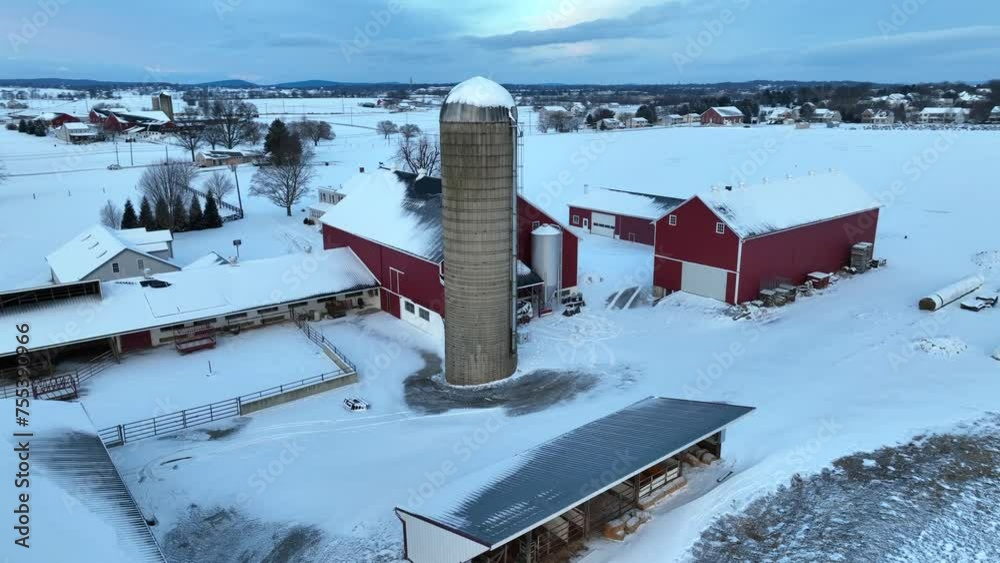 Snowy farm with red barns, a silo, and bare trees under a cloudy sky ...