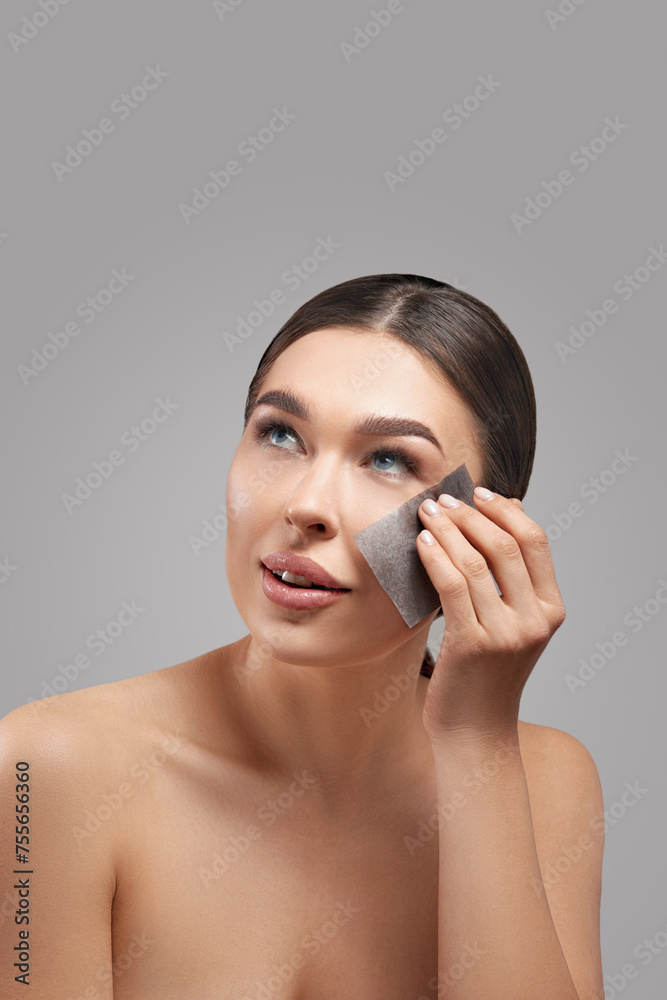 Skin care. Young woman removing oil from face using blotting papers ...