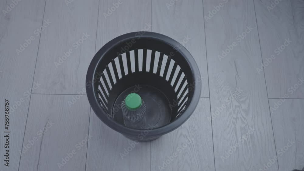Plastic bottle falling into small black garbage bin on white parquet ...