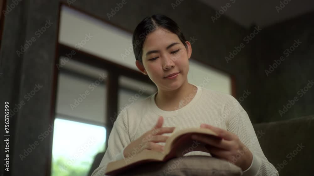 Young happy beautiful asian woman reading a book on cozy couch at ...