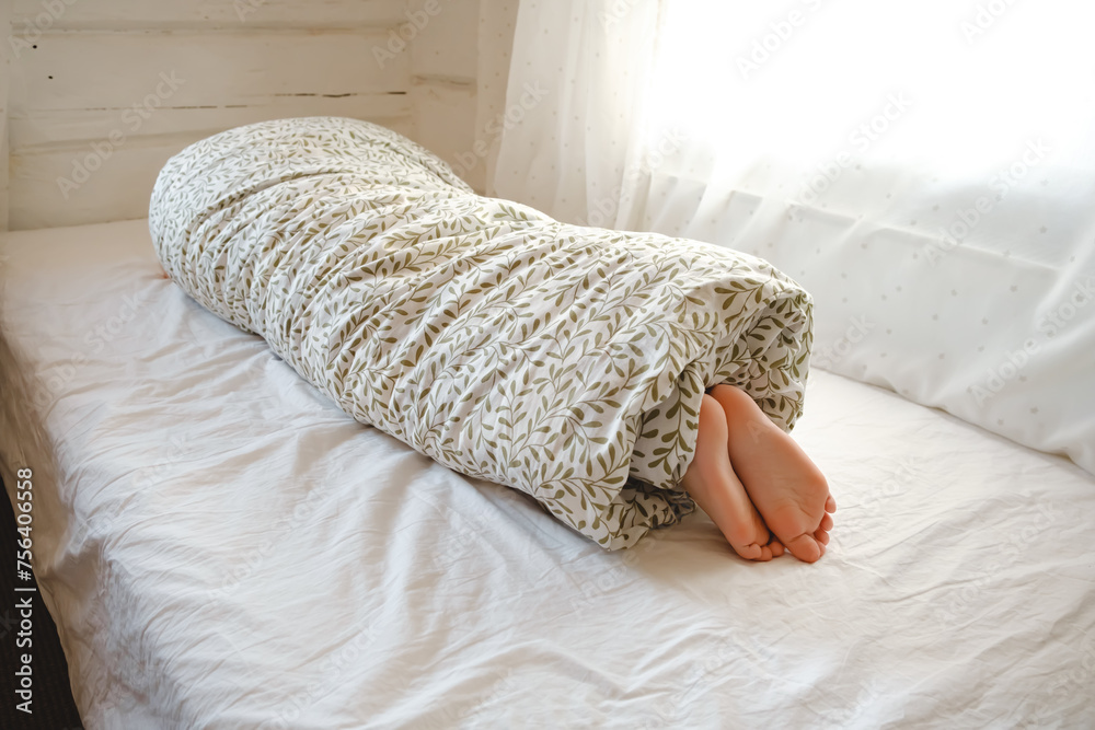 Rolled person. A child wrapped in a blanket with sticking out feet lies ...