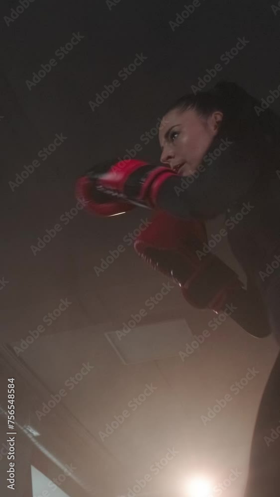 Strong, aggressive female fighter kicks a punching bag. Sporty angry ...