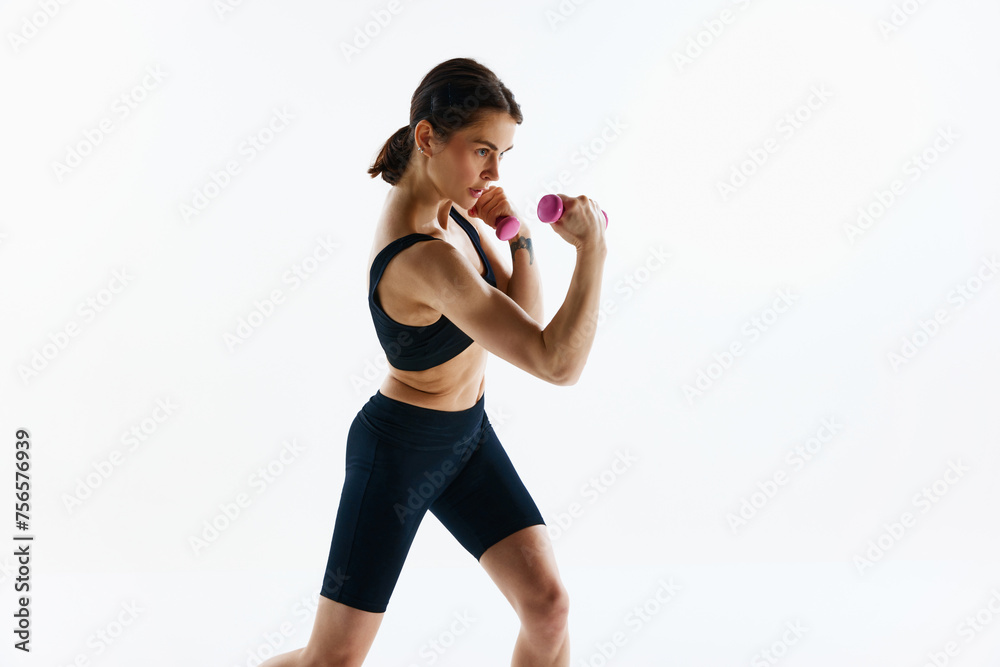 Young woman with sportive body training, doing uppercut with dumbbells ...