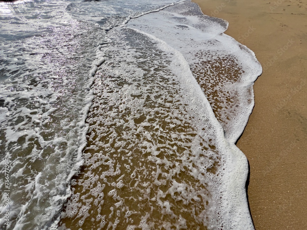 Detail of wave breaking on golden sand. Overlapping layers of foaming ...