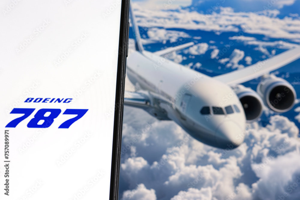 Boeing 787 logo is sharp in the foreground, while flying airplane is ...
