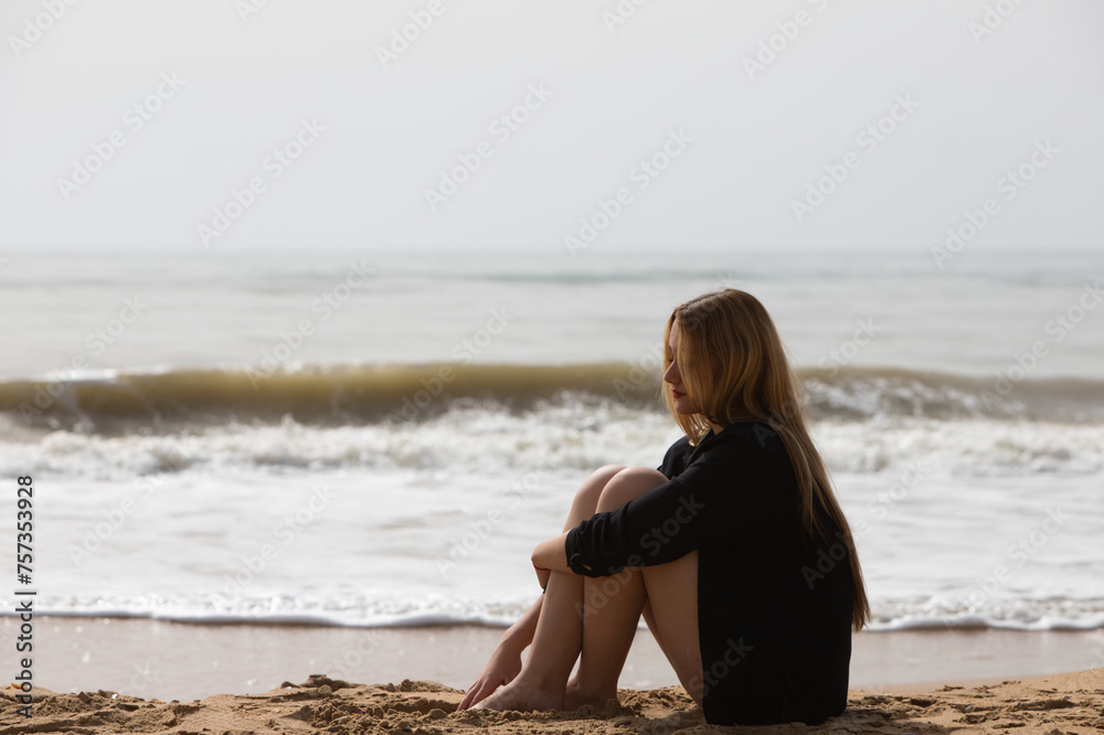 Beautiful young blonde woman in black shirt sits on the shore of the ...