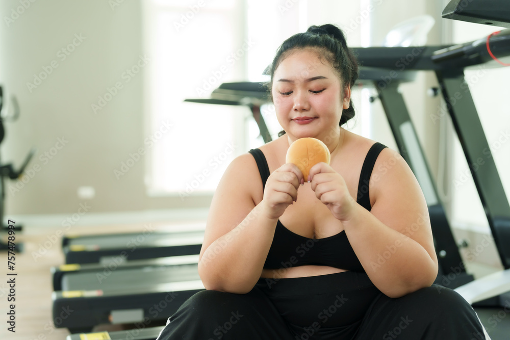 Overweight Asian woman exercise in gym, female contemplates her snack ...