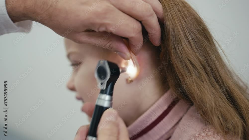 Close-up. A male pediatrician doctor uses an otoscope to conduct a ...