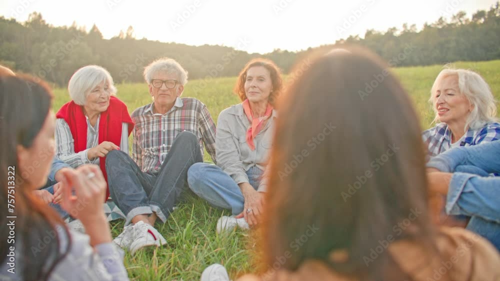 Group of differently aged people sit together on hill. Multi-ethnic ...