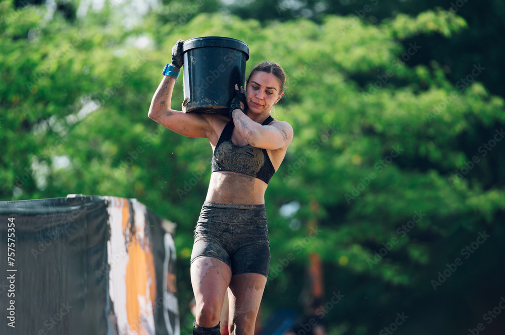 Female participating in an OCR race while carrying heavy barrel on her ...