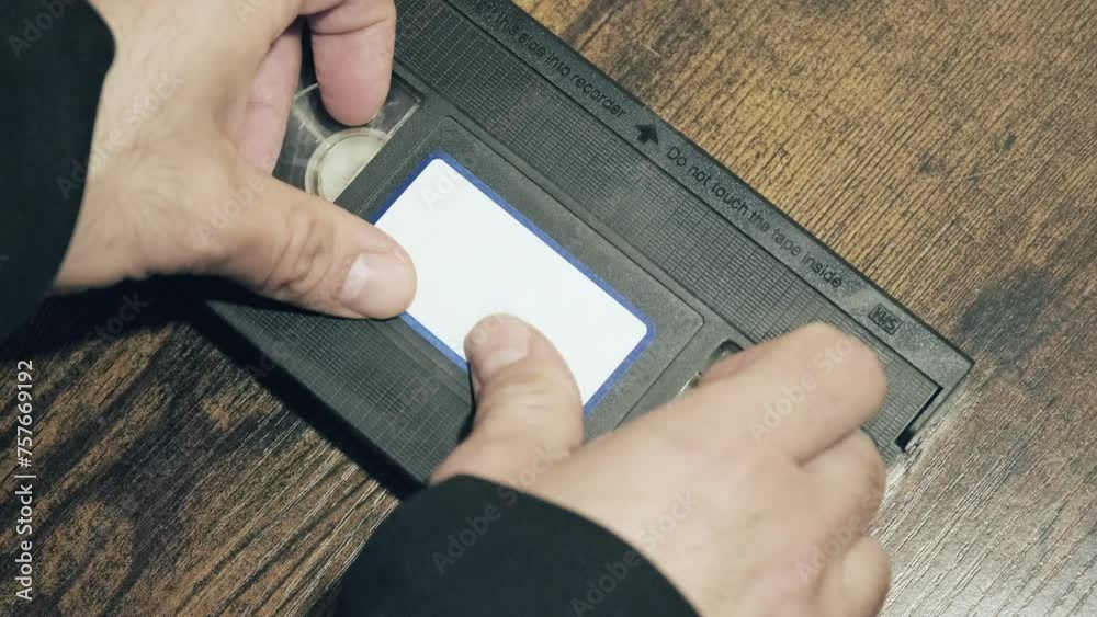 Hands sticking a blank empty label on the front side of a vintage VHS ...