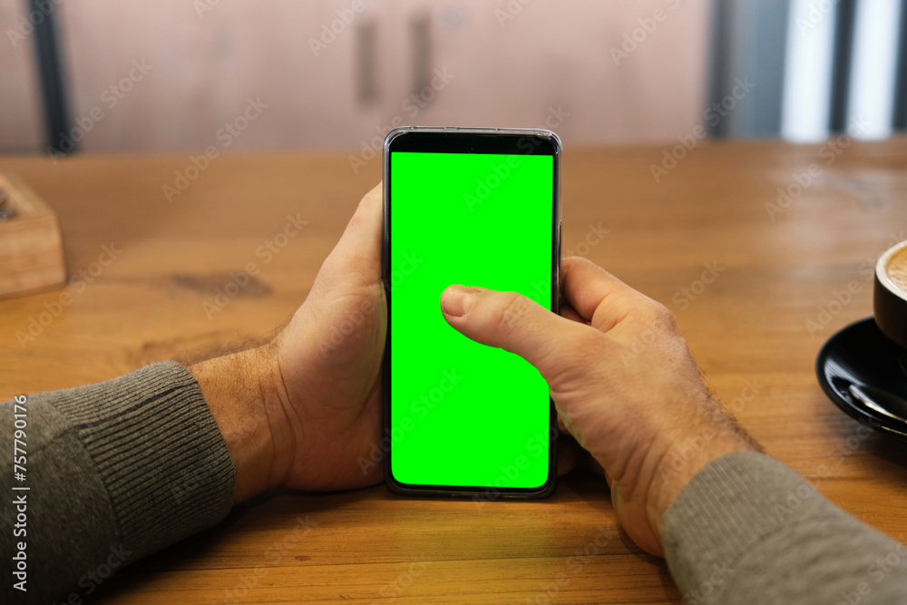 Young man sitting at cafe holding smartphone green mock-up screen in ...