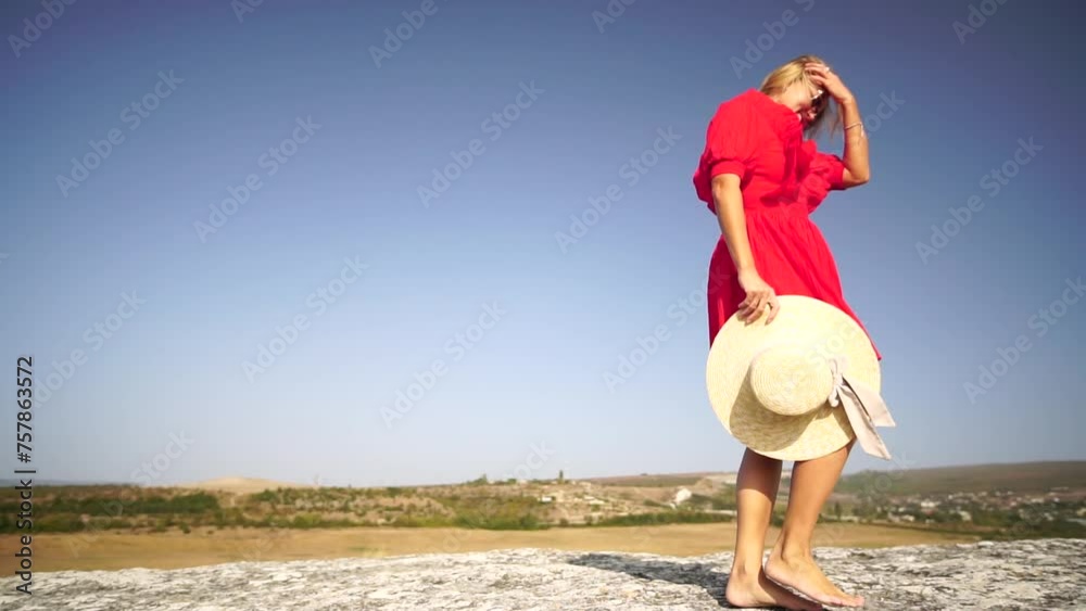woman in a red dress and straw hat standing on a rock, enjoying the ...