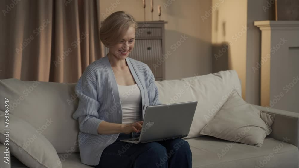 A joyful woman is seated on a sofa with a laptop on her knees, clapping ...