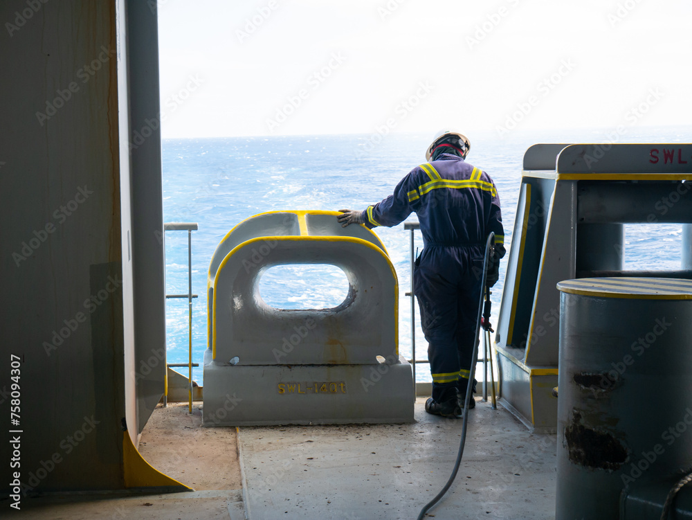 Able seaman crew member of cargo vessel is chipping rust from the ship ...