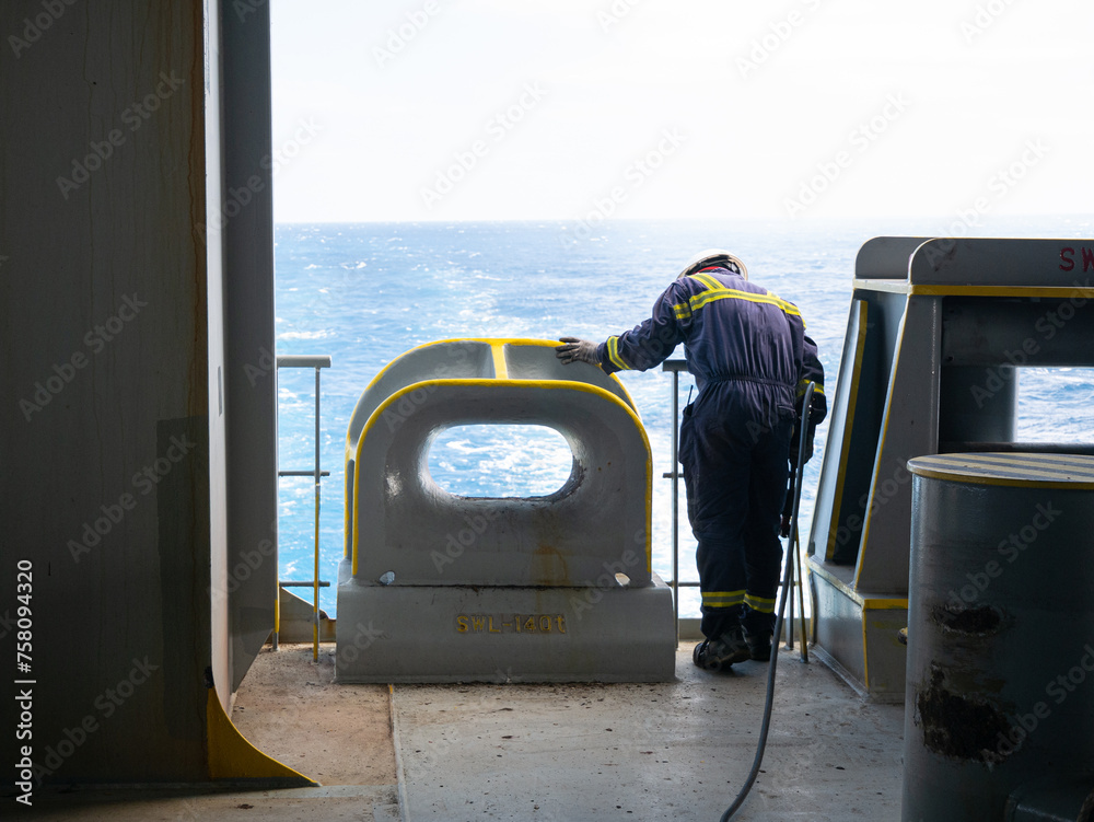 Able seaman crew member of cargo vessel is chipping rust from the ship ...