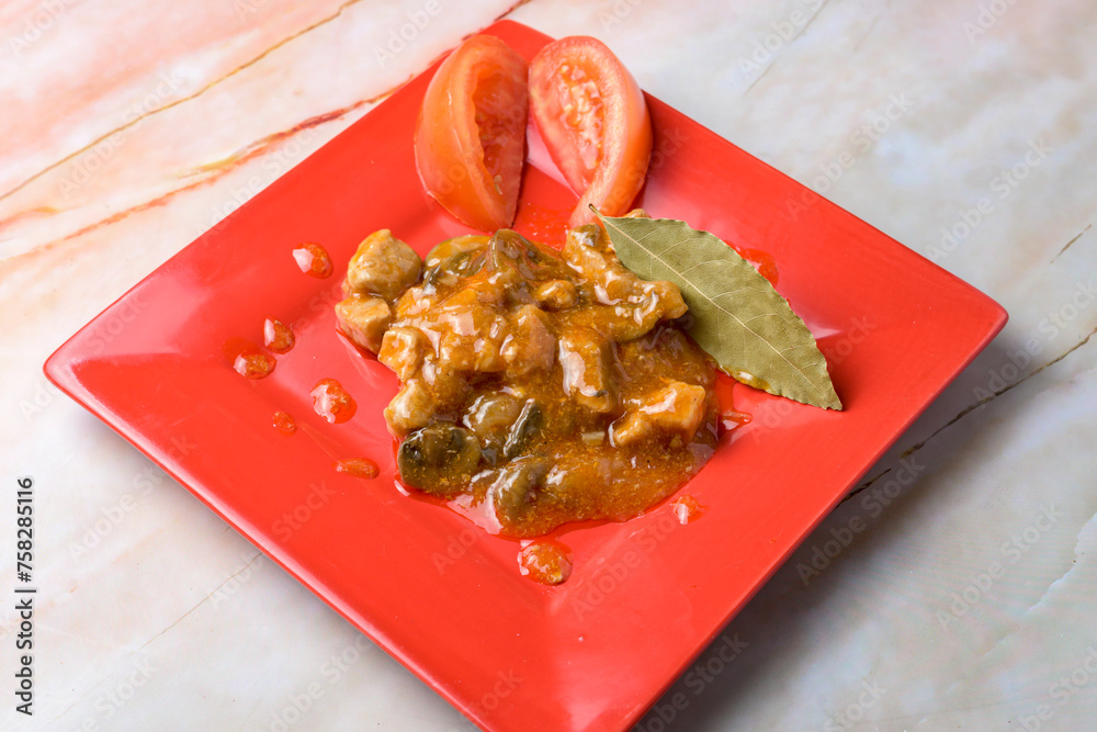 Pork stew with a bay leaf and tomato garnish on a red plate, marble ...