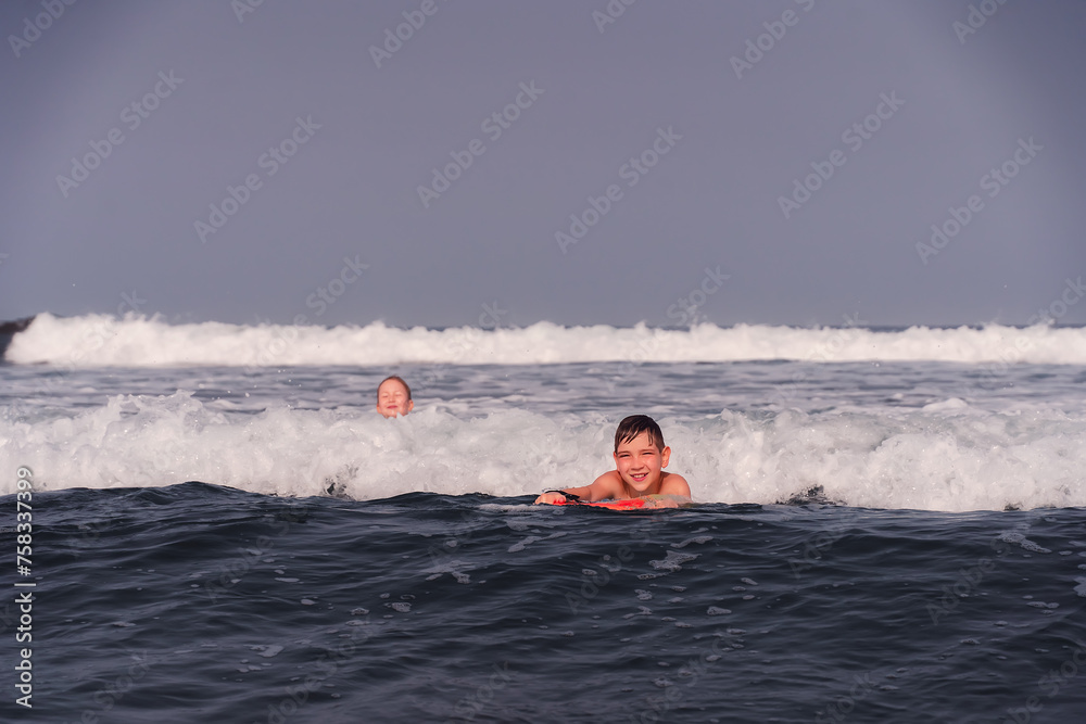 Two children enjoy the ocean, one with a bright smile floating on a ...