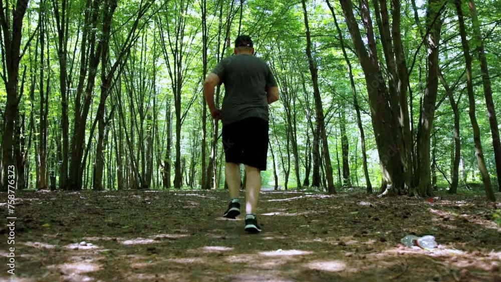 An overweight and fat man runs along a forest path in a park in the ...