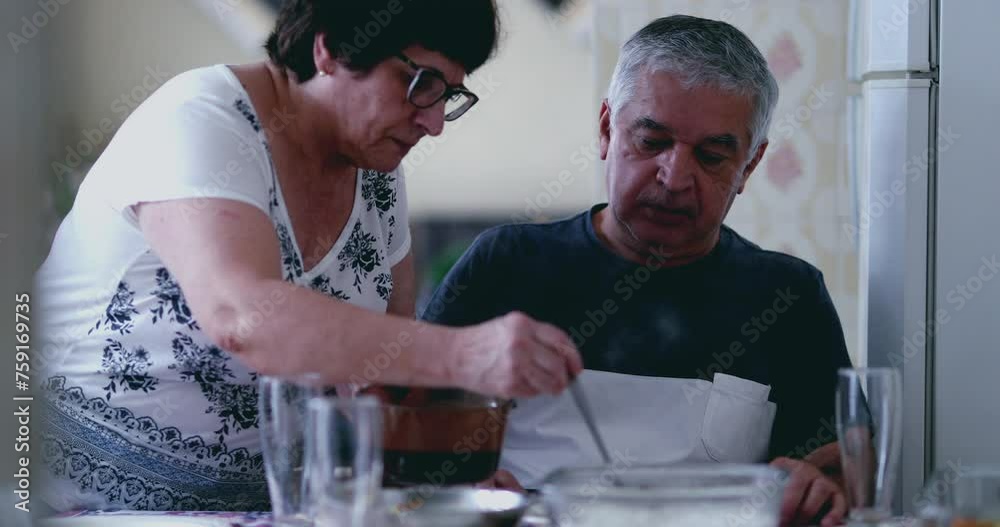 Senior spouse serving husband food during lunch time, depicting ...