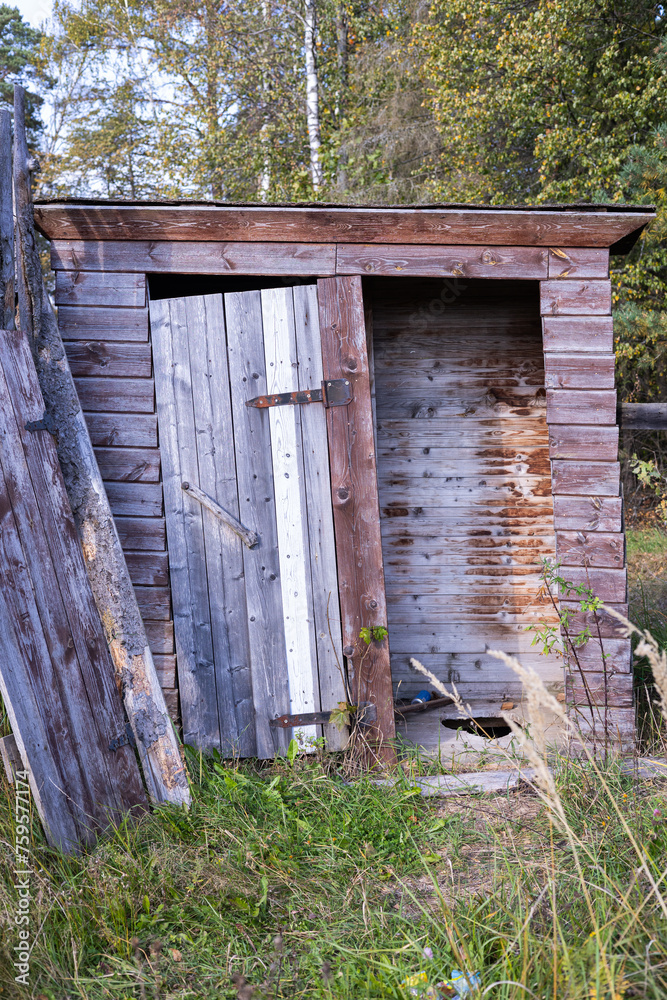 An old, rickety village toilet stands on the street among the trees. Wooden old toilet on the ...