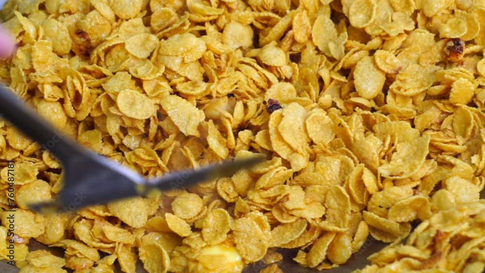 A hand mixing of cornflakes with honey on big pan in the making of ...