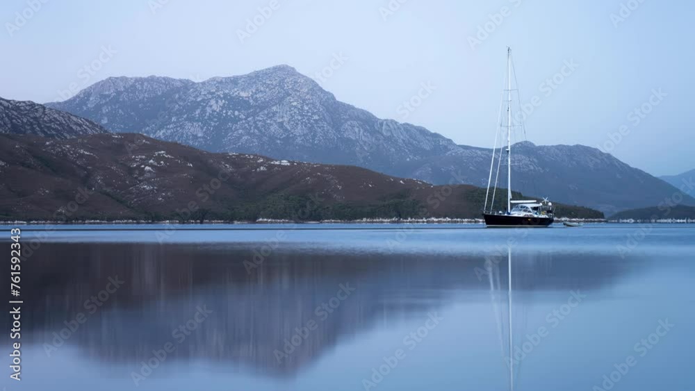 time lapse of a yacht and boat under clouds over mountains over the ...