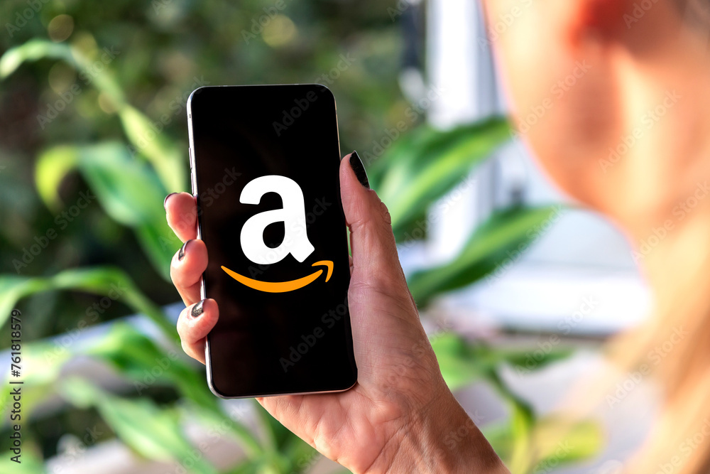 Amazon logo in the screen of mobile phone. Blonde woman with smartphone ...