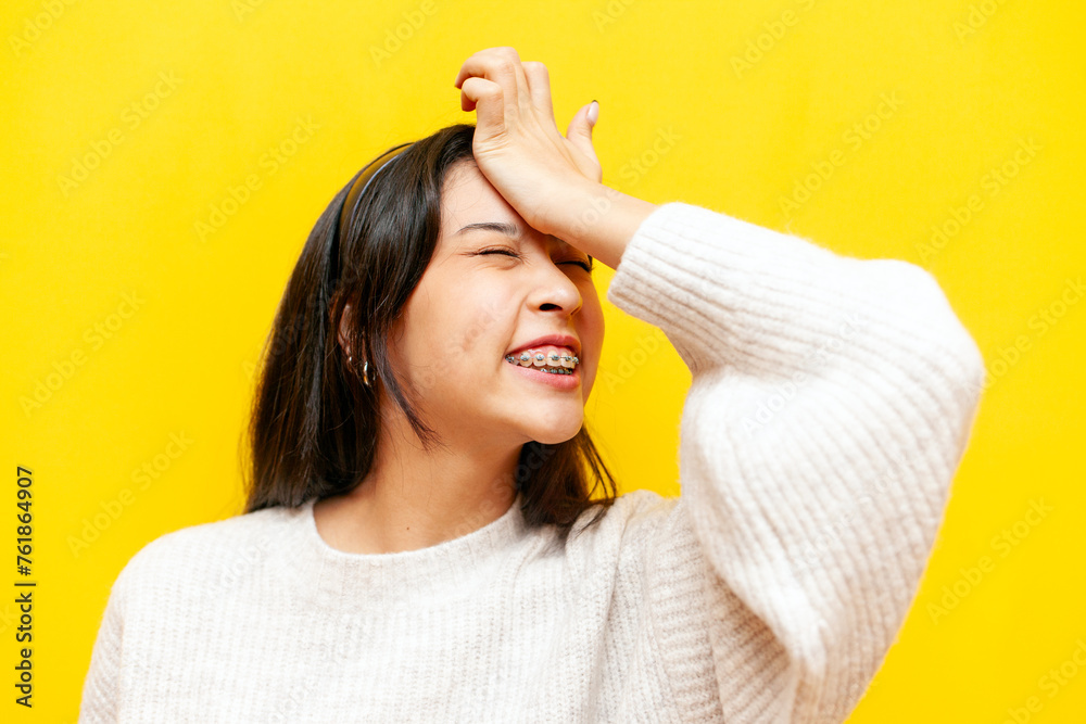 young dissatisfied asian woman with braces shows facepalm on yellow ...
