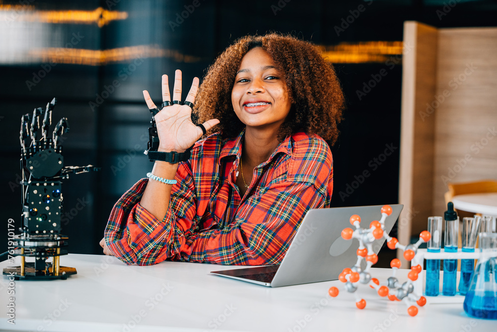 Black teenage student in a classroom learns and tests a robotic arm on ...