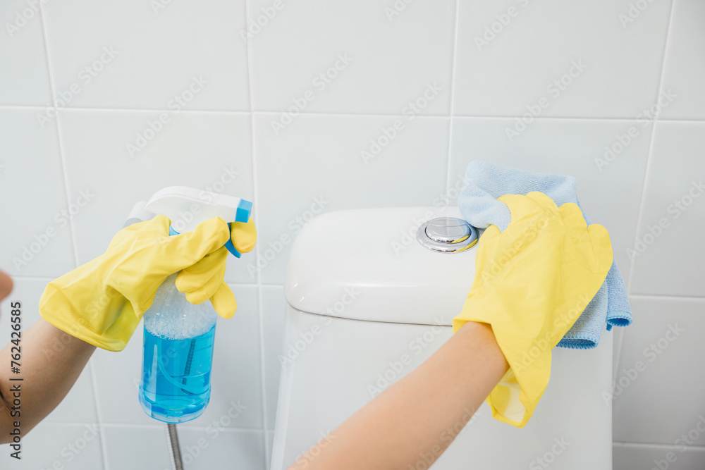 Maid in yellow gloves meticulously cleans the toilet seat in restroom ...