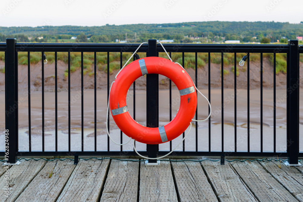 A vibrant orange polyethylene life ring hangs on a black metal railing ...