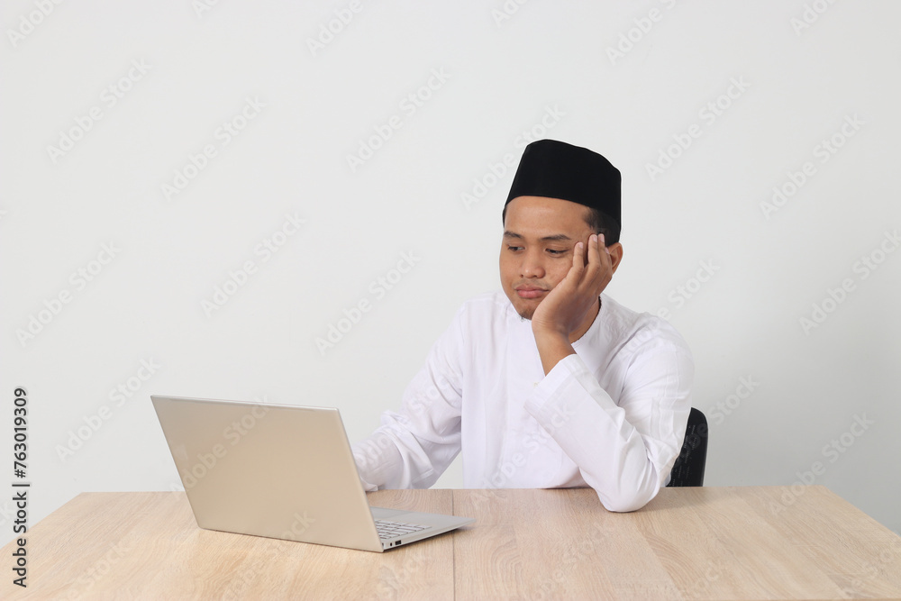 Portrait of tired Asian muslim man in koko shirt with skullcap working ...